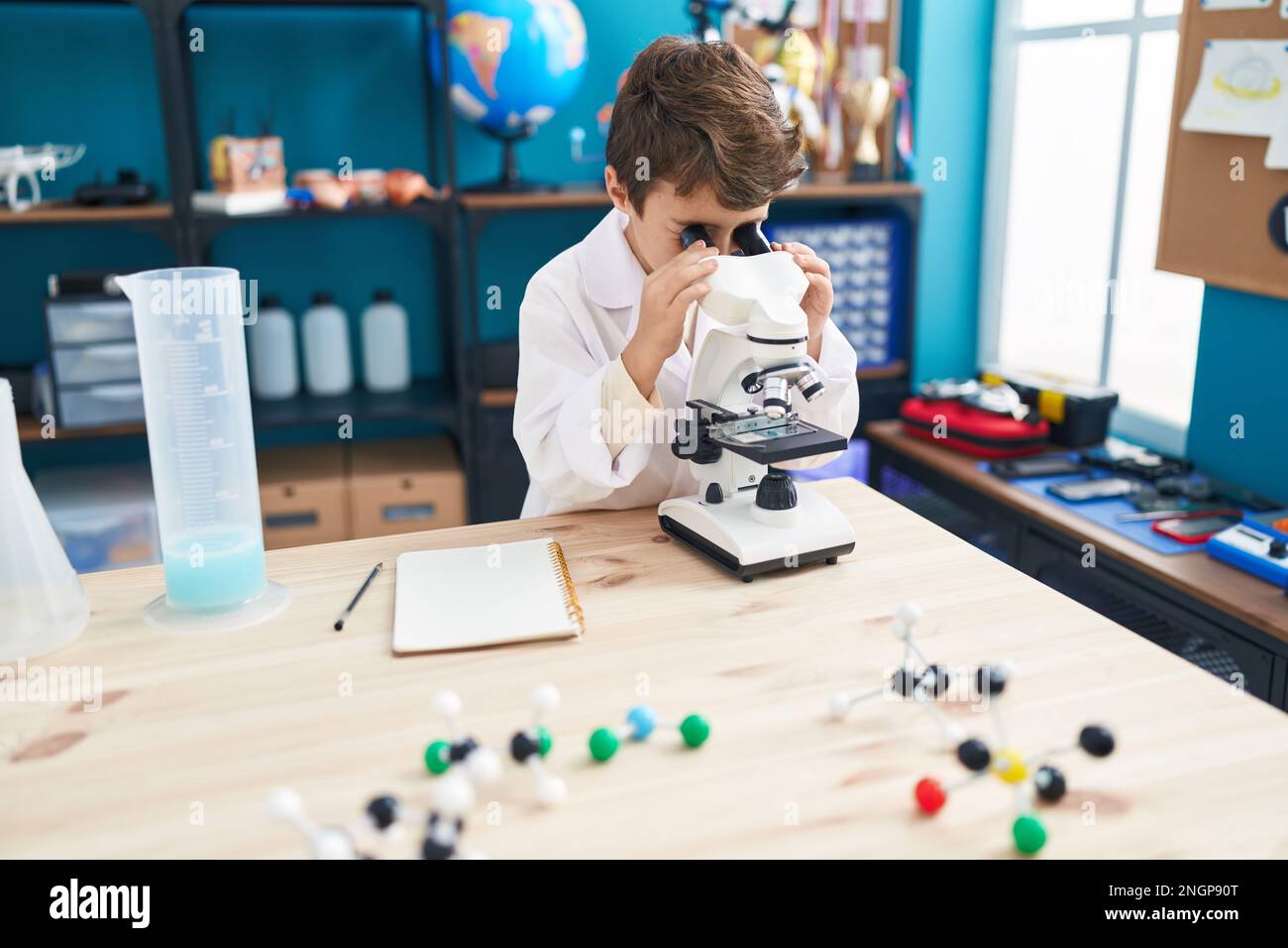 Adorable hispanic boy student using microscope at laboratory classroom ...