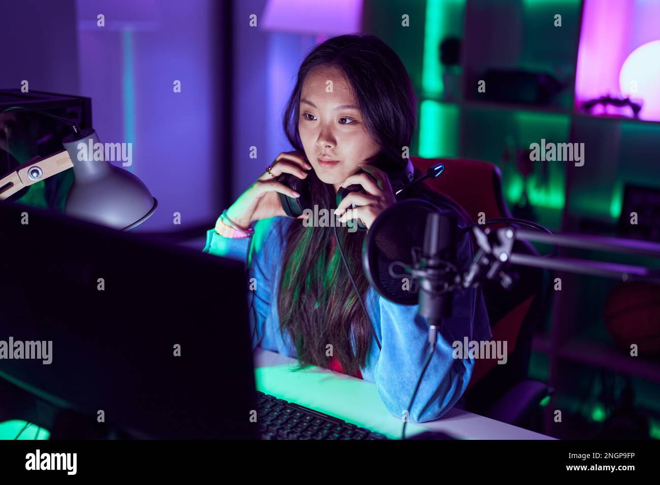 Young chinese woman streamer using computer holding headphones at ...