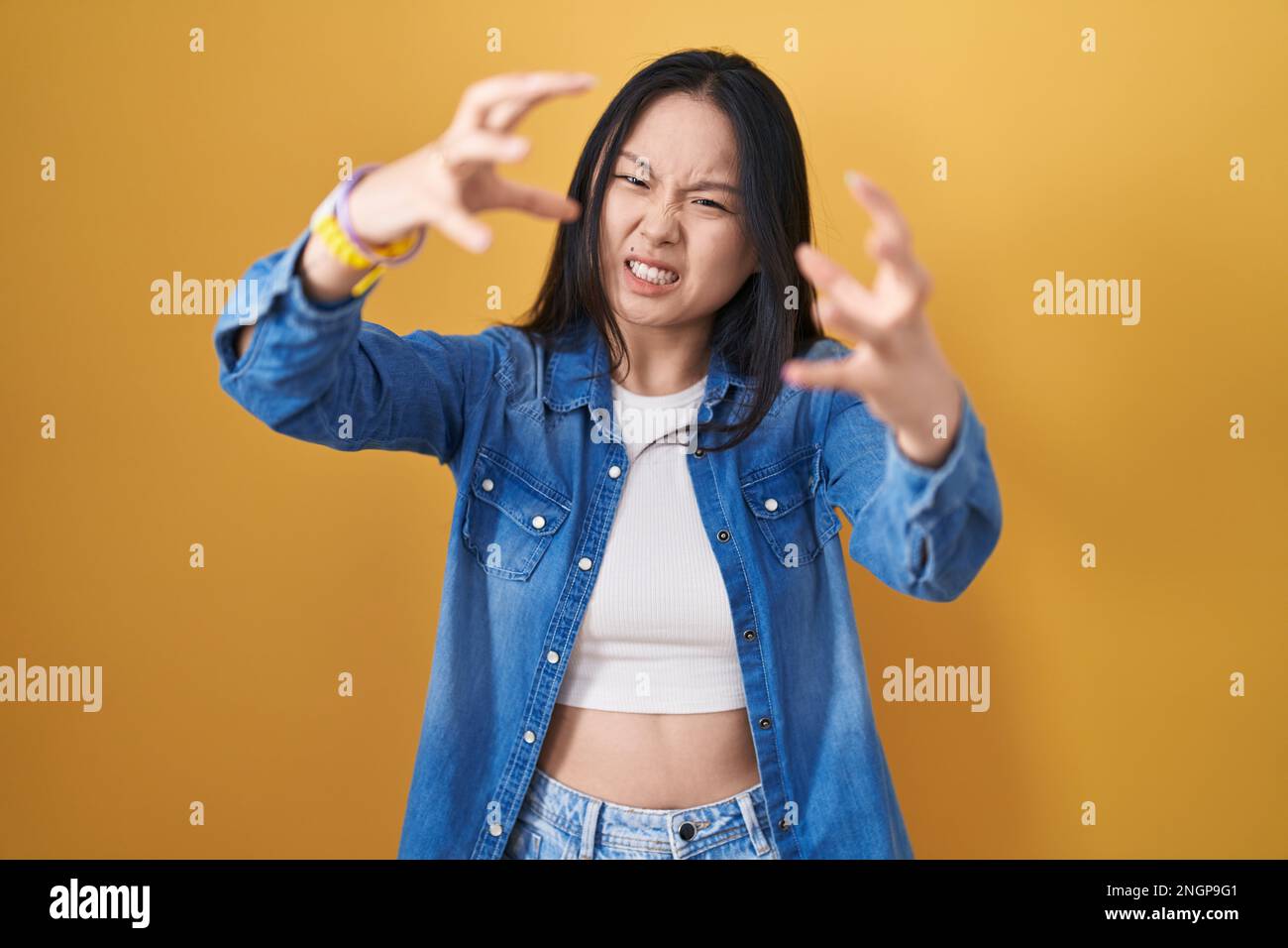 Young asian woman standing over yellow background shouting frustrated ...