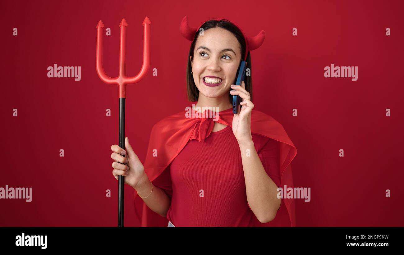 Young beautiful hispanic woman wearing devil costume talking on ...