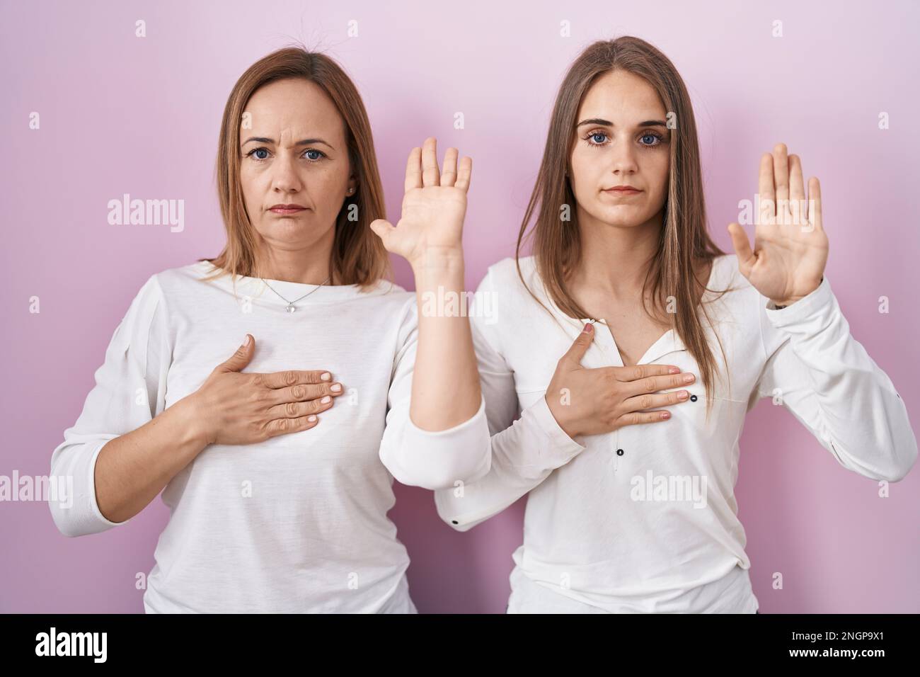 Middle age mother and young daughter standing over pink background ...