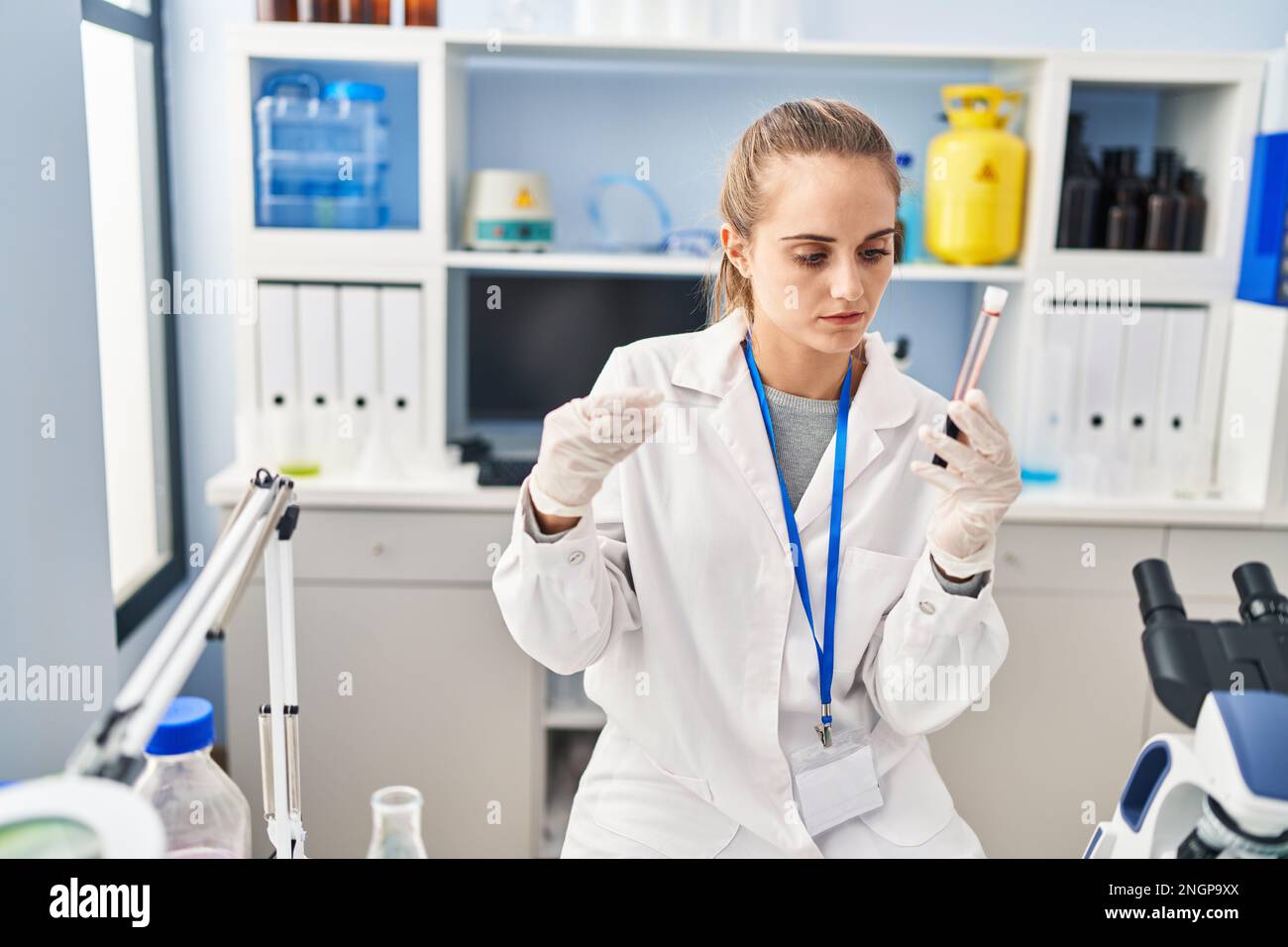 Young blonde woman wearing scientist uniform analysing blood at ...
