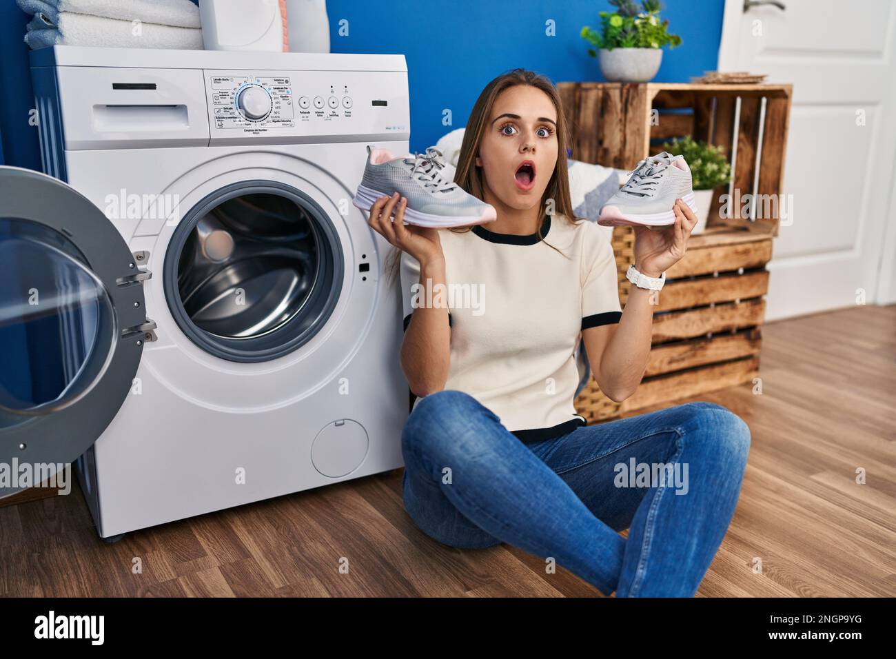 Young woman putting sneakers in washing machine afraid and shocked with ...