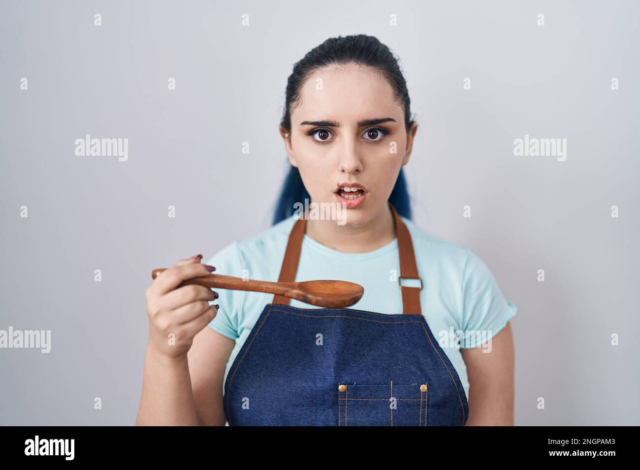 Young modern girl with blue hair wearing cook apron holding spoon ...