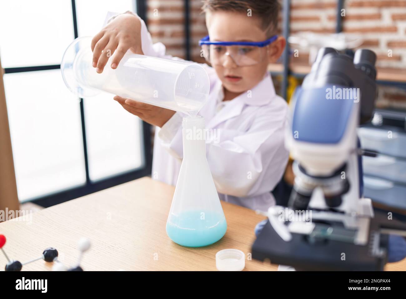 Adorable hispanic boy student pouring liquid on test tube at laboratory ...