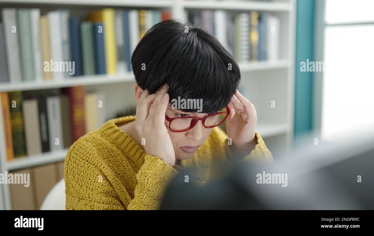 Young chinese woman student using computer stressed at library ...