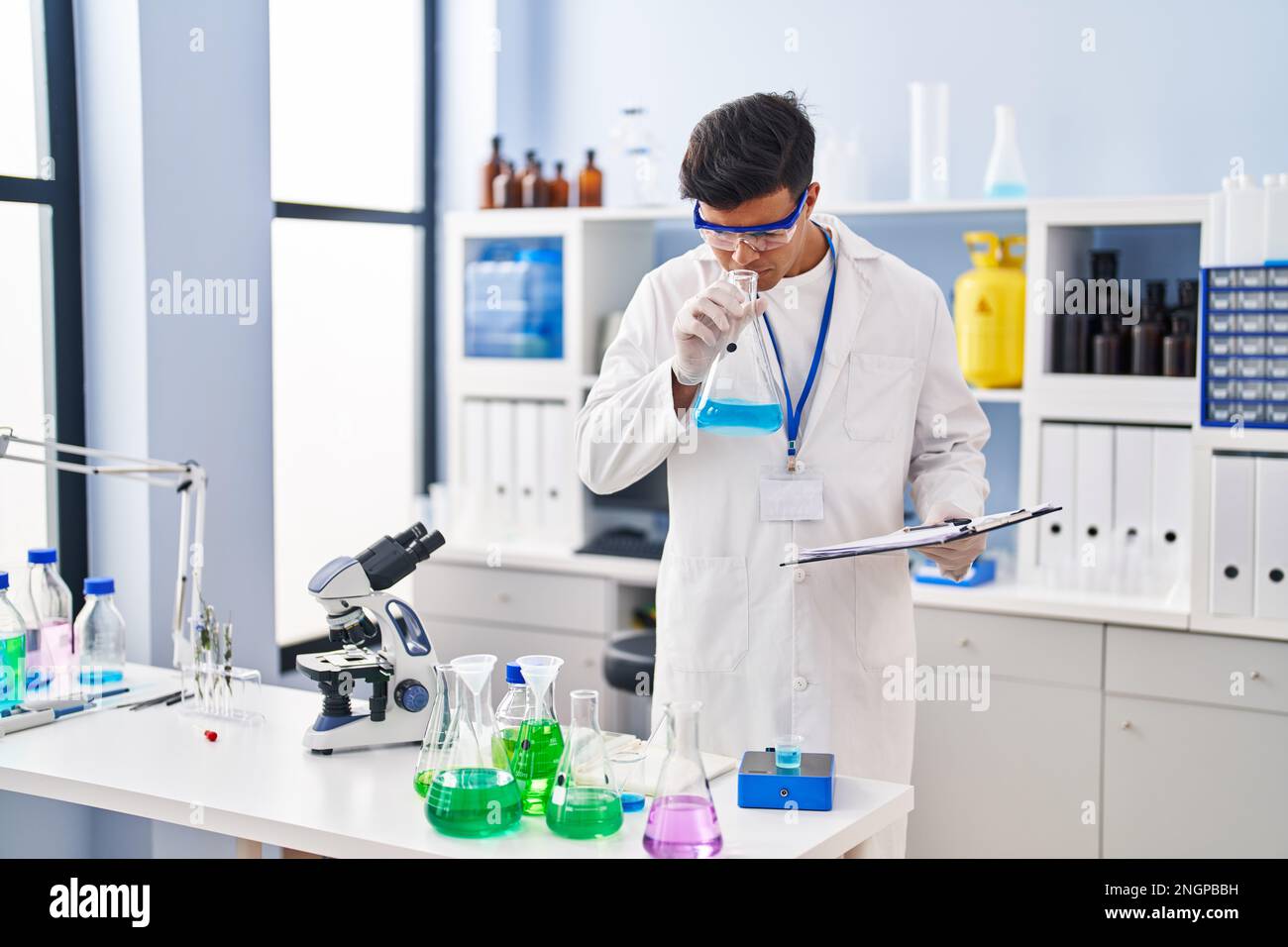 Young hispanic man scientist smelling liquid on test tube at laboratory ...