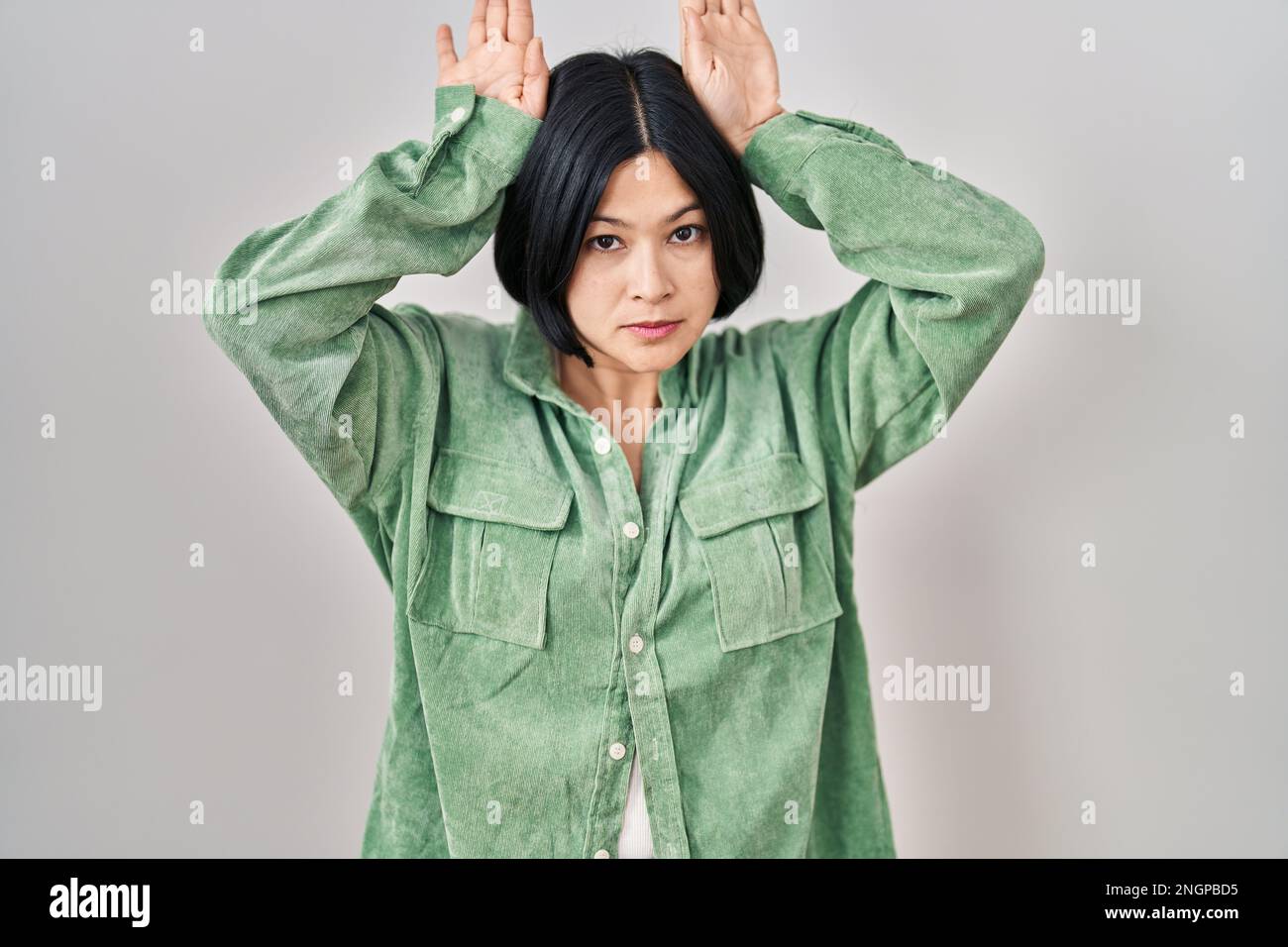 Young asian woman standing over white background doing bunny ears ...
