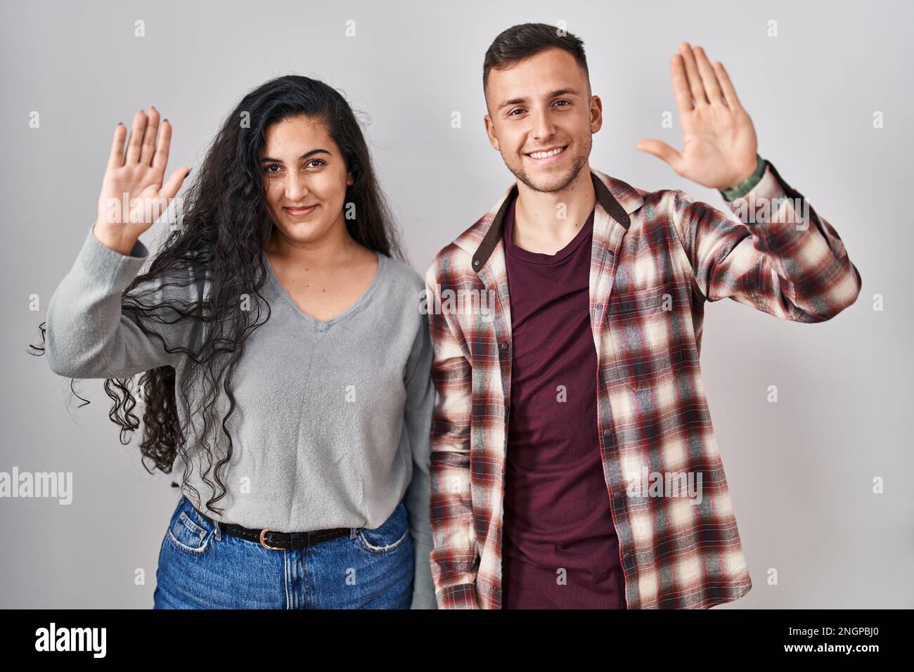 Young hispanic couple standing over white background waiving saying ...