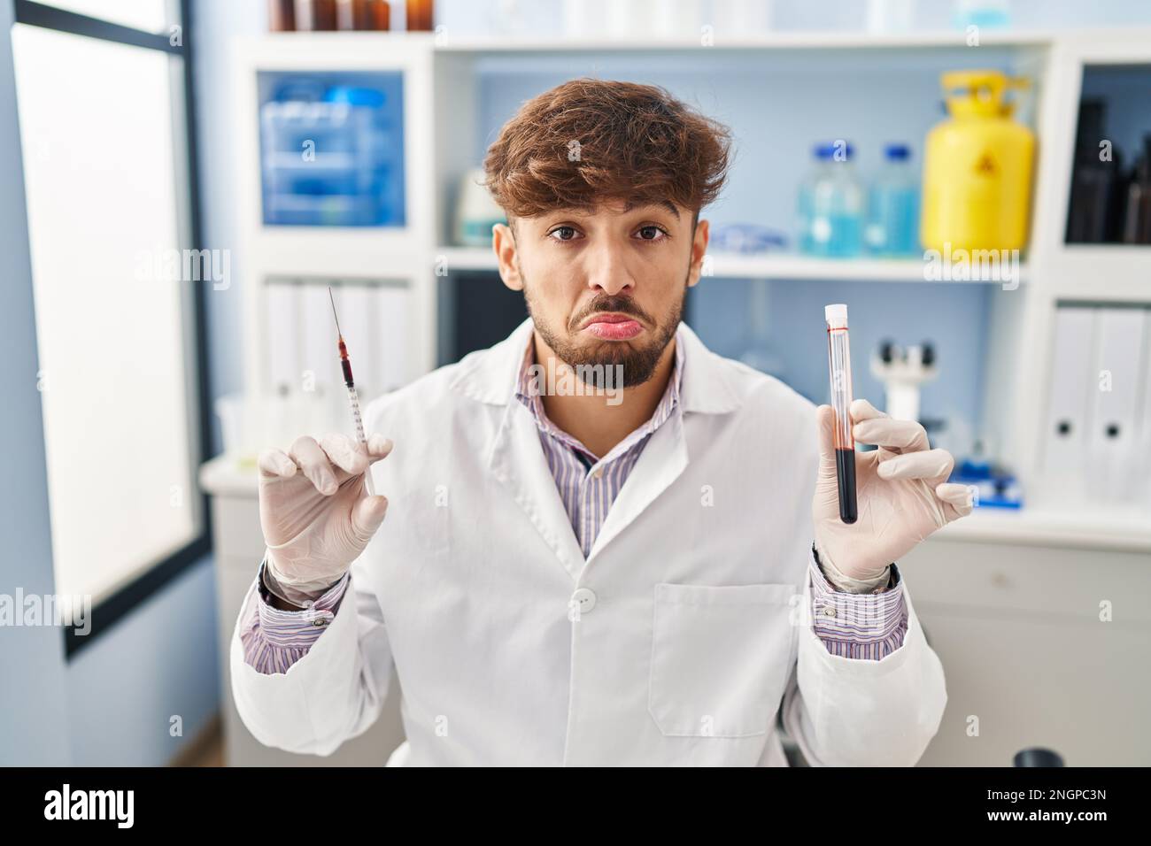 Arab man with beard working at scientist laboratory holding blood sample depressed and worry for ...
