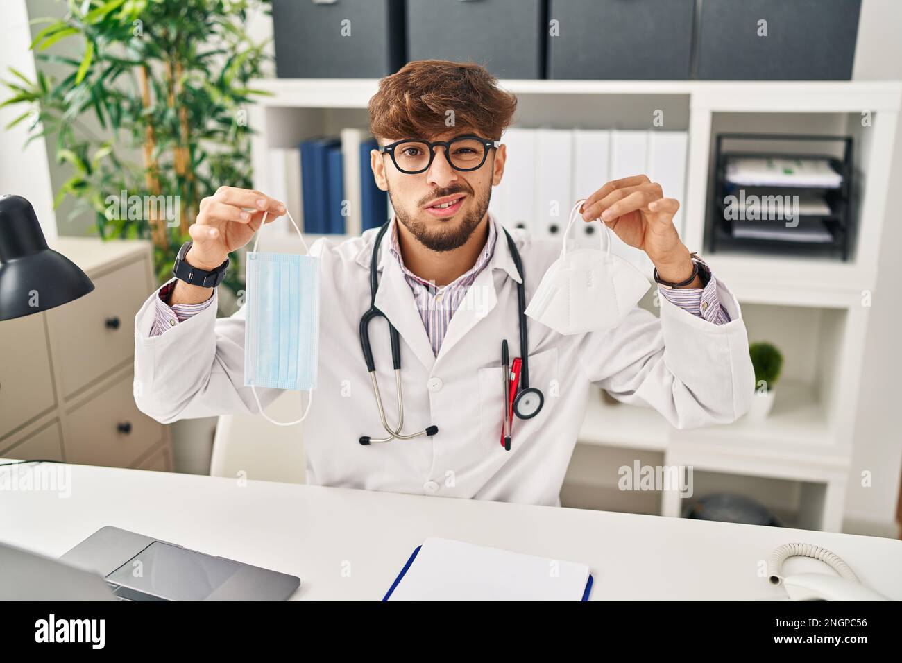 Arab man with beard wearing doctor uniform holding medical mask ...