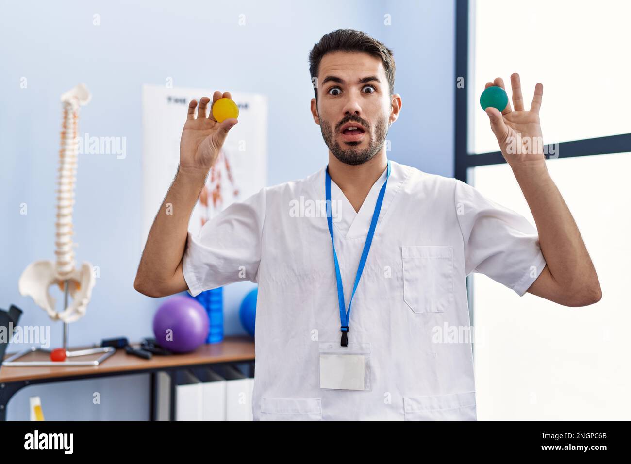 Young hispanic physiotherapist man holding strength balls to train hand ...