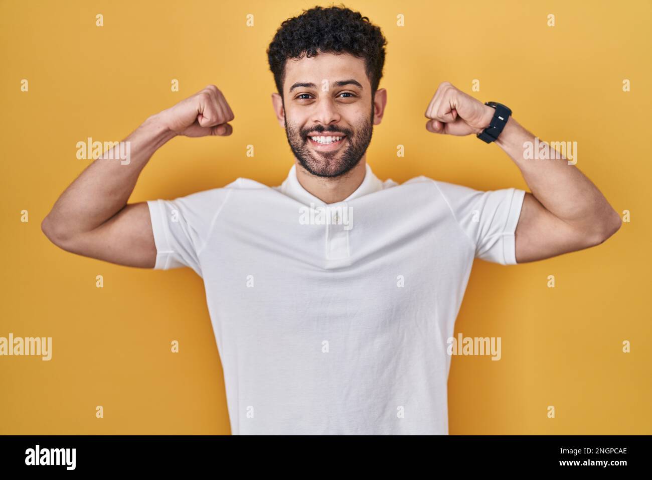 Arab man standing over yellow background showing arms muscles smiling ...