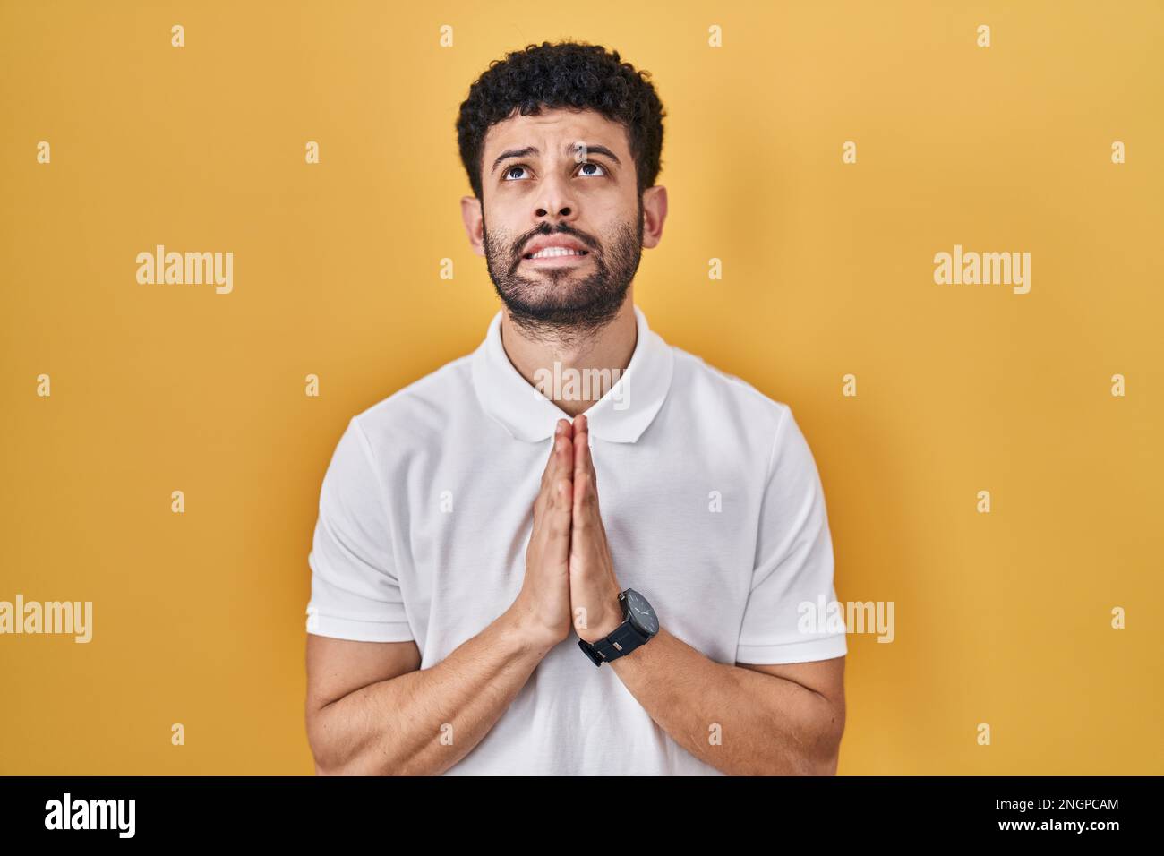 Arab man standing over yellow background begging and praying with hands ...