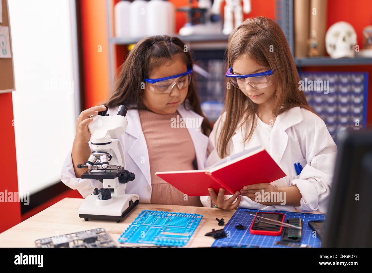 Two kids students using microscope reading notebook at laboratory ...