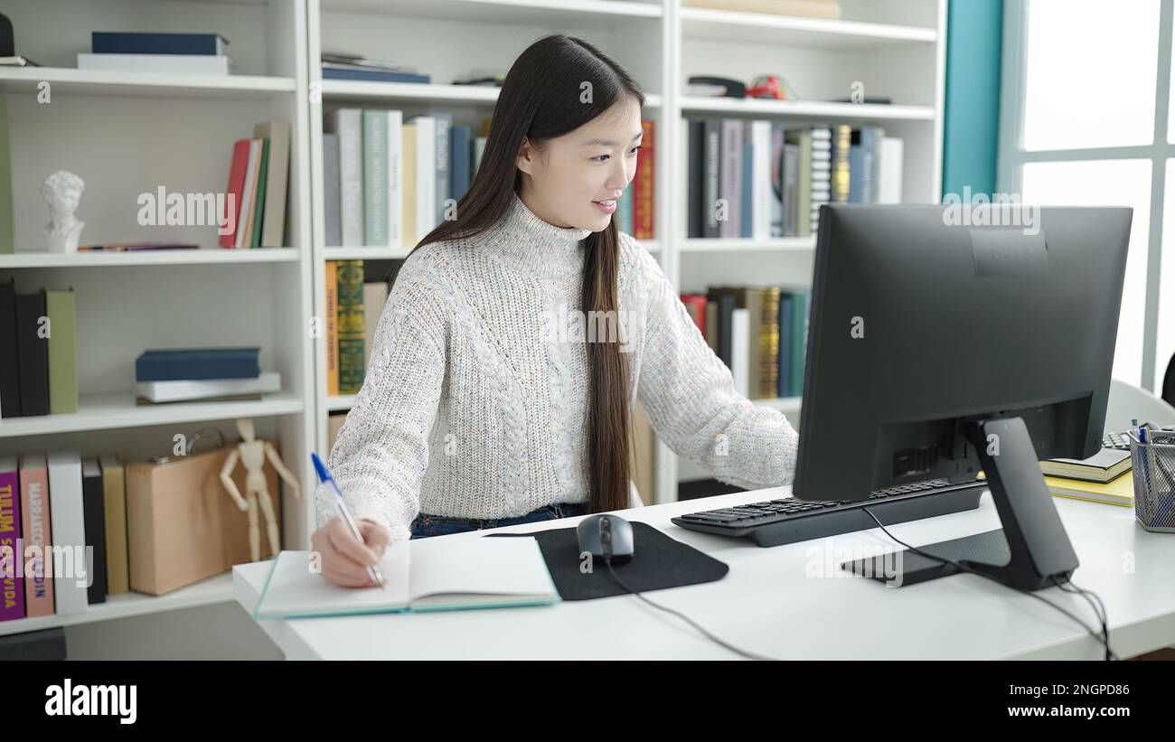 Young chinese woman student using computer writing on notebook at ...