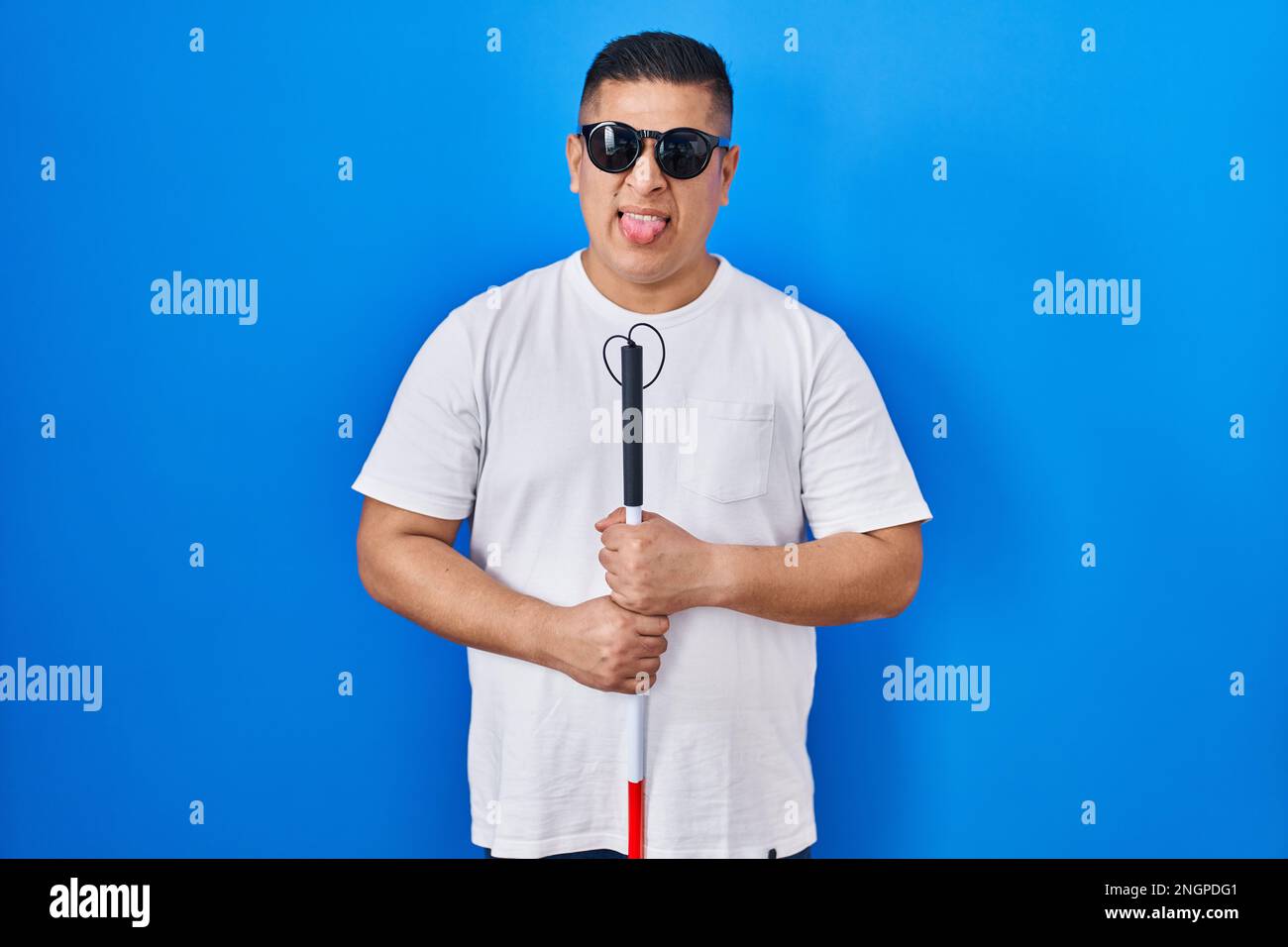 Hispanic young blind man holding cane sticking tongue out happy with ...