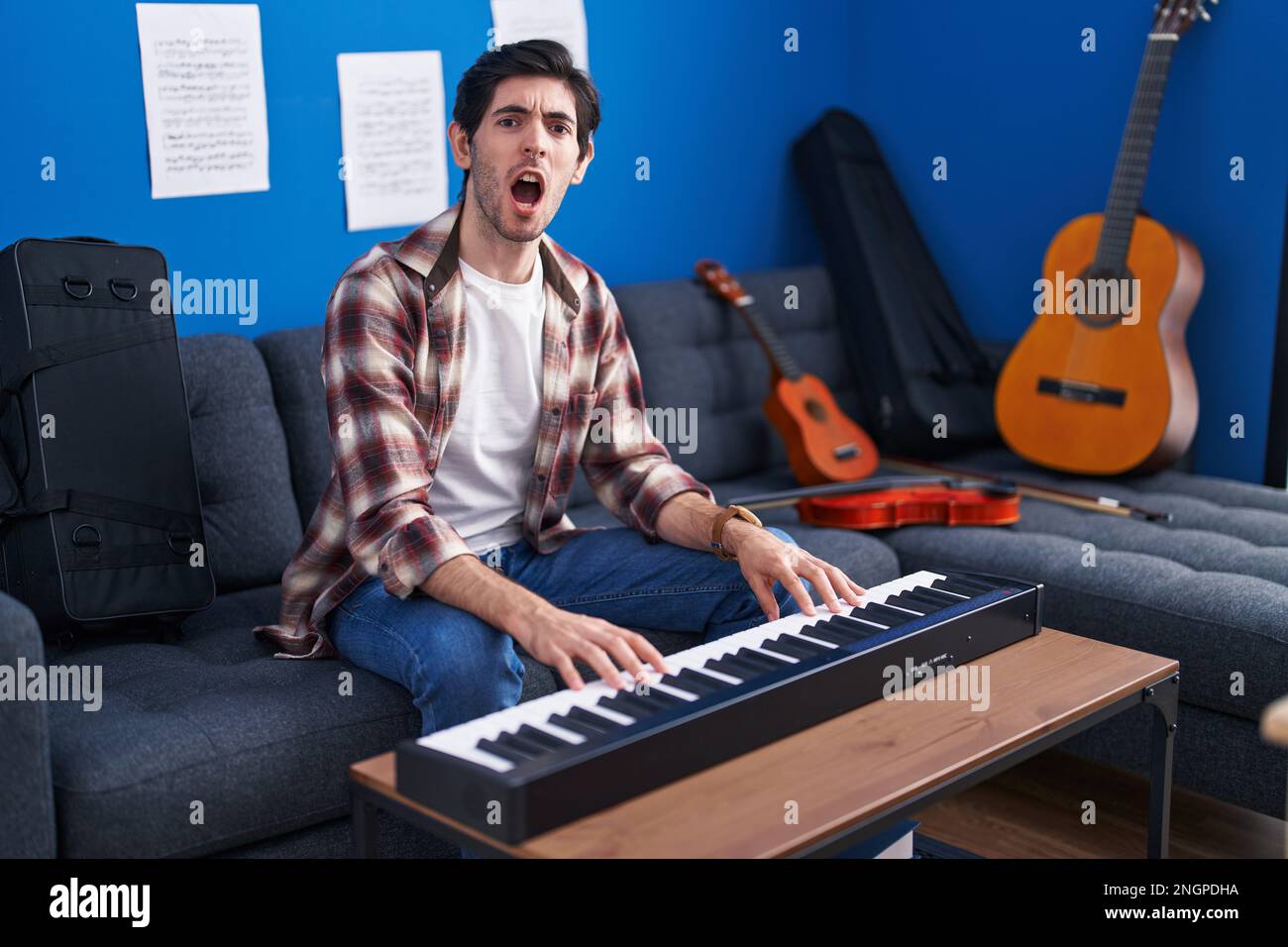 Young hispanic man playing piano at music studio angry and mad ...