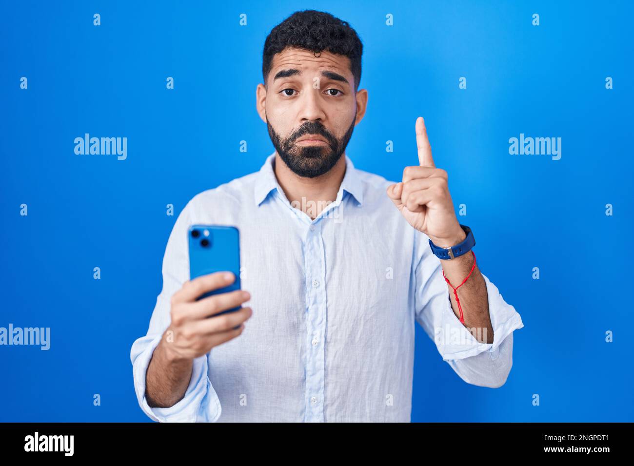 Hispanic man with beard using smartphone typing message pointing up ...