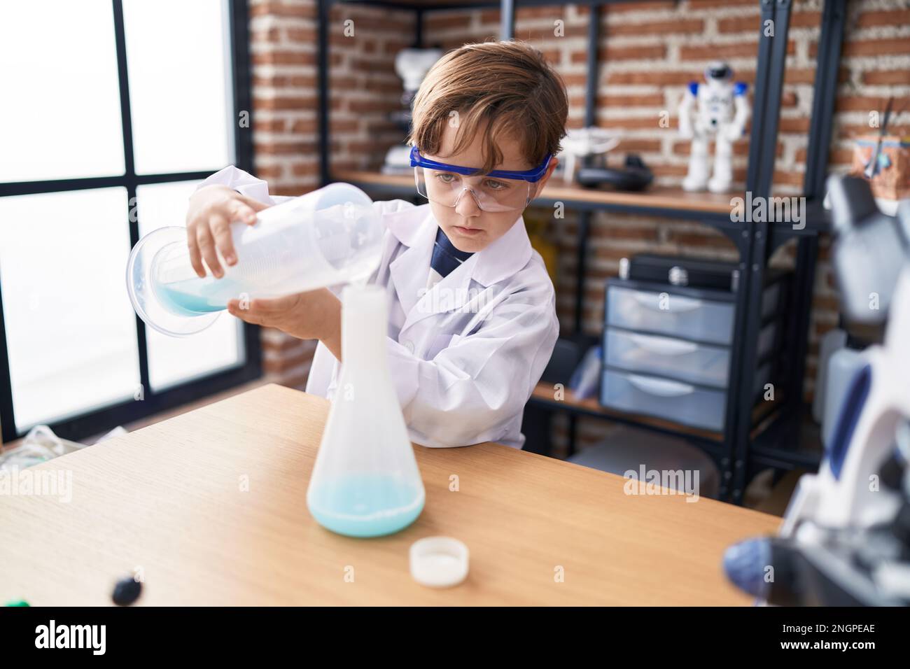 Adorable hispanic boy student pouring liquid on test tube at laboratory ...