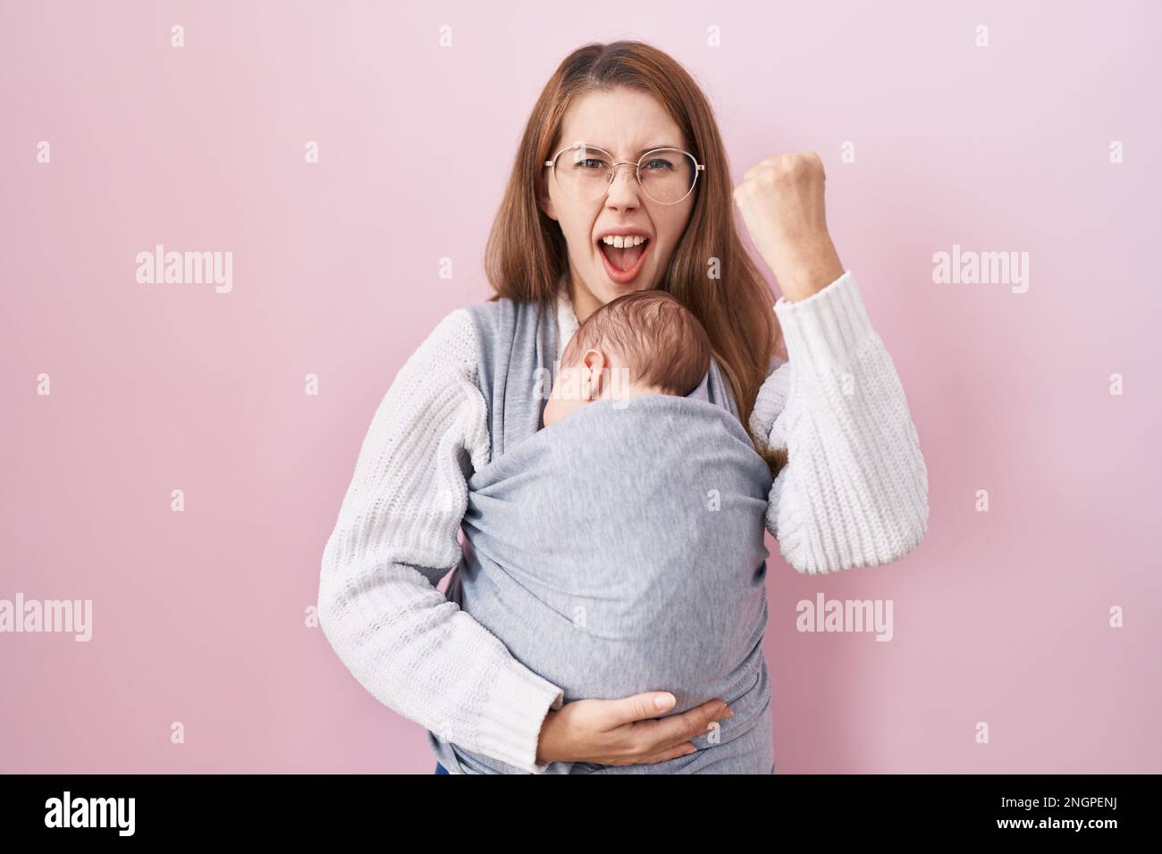 Young caucasian woman holding and carrying baby on a sling annoyed and ...