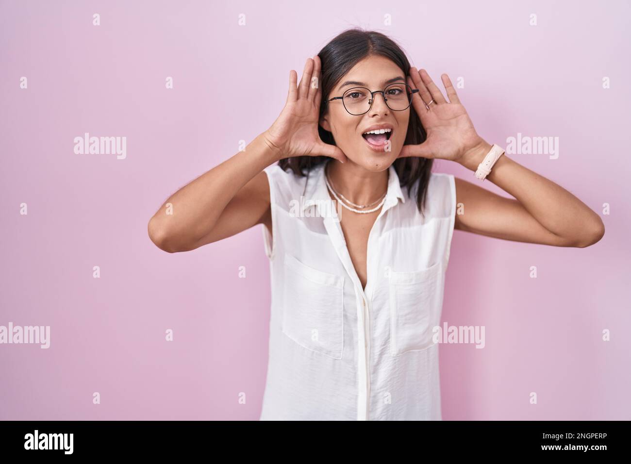 Brunette young woman standing over pink background wearing glasses ...