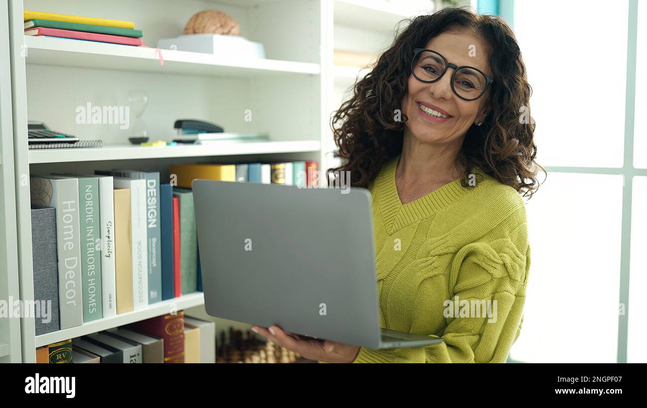 Middle age hispanic woman teacher using laptop studying at library university Stock Photo - Alamy