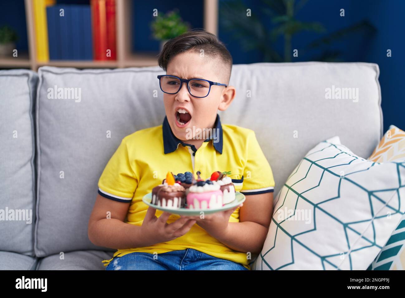 Young hispanic kid holding cake sweets angry and mad screaming ...