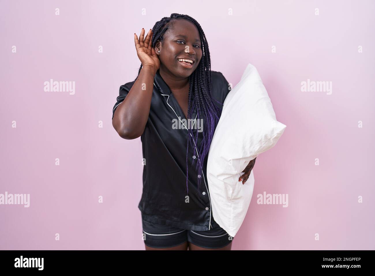 Young african woman wearing pijama hugging pillow smiling with hand ...