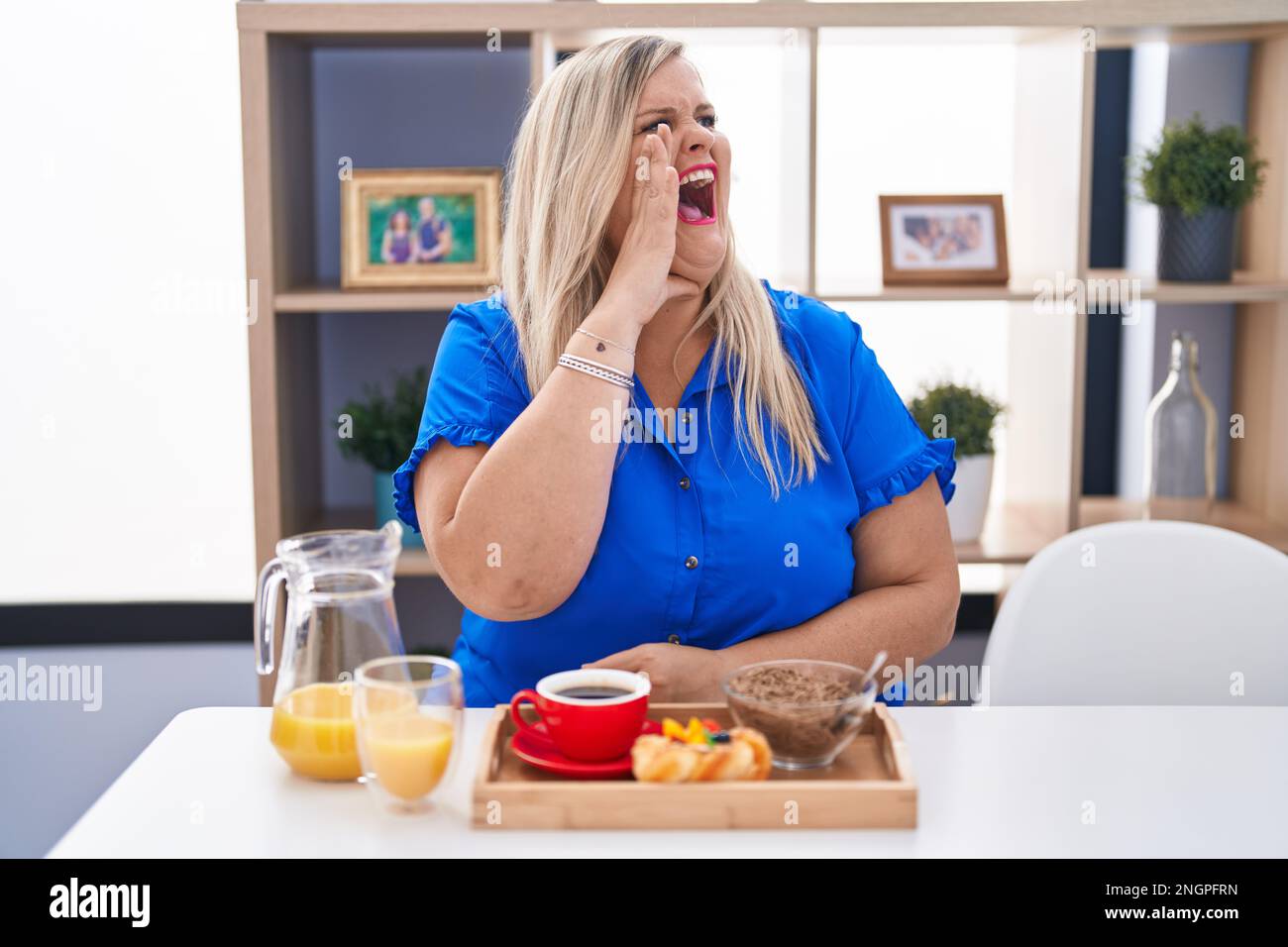 Caucasian plus size woman eating breakfast at home shouting and ...