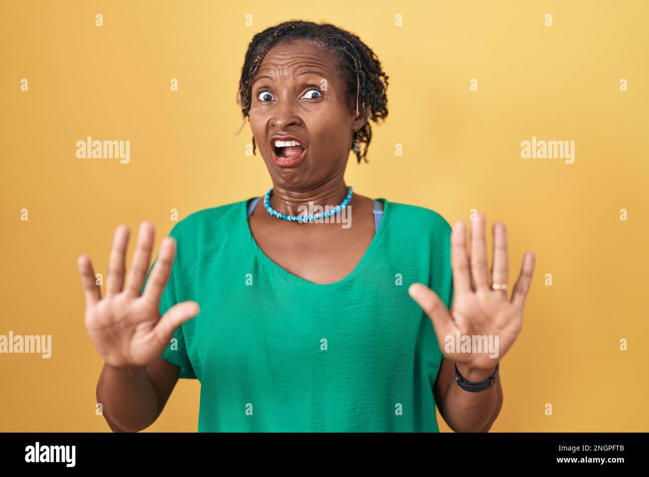 African woman with dreadlocks standing over yellow background afraid ...