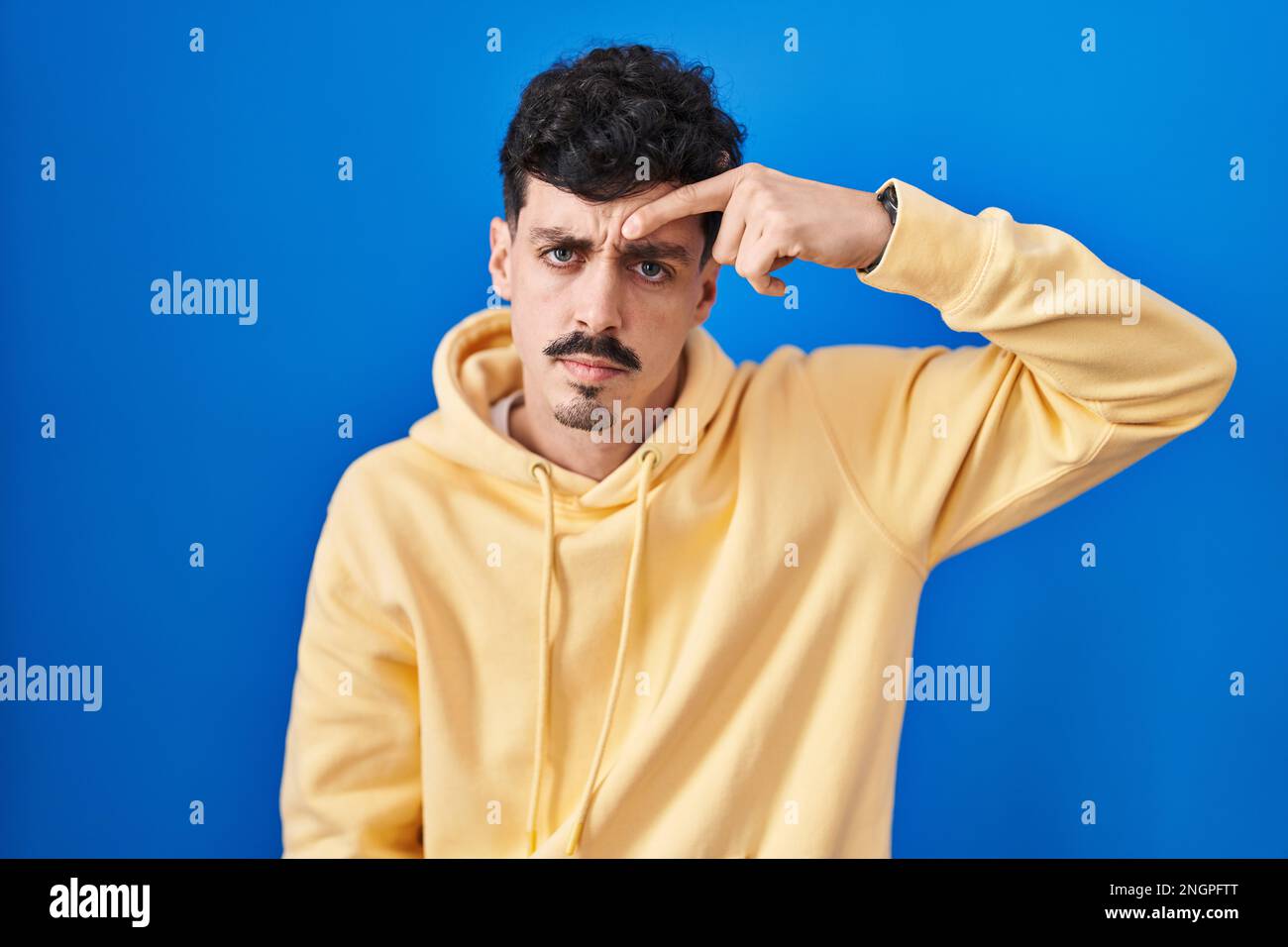 Hispanic man standing over blue background pointing unhappy to pimple ...