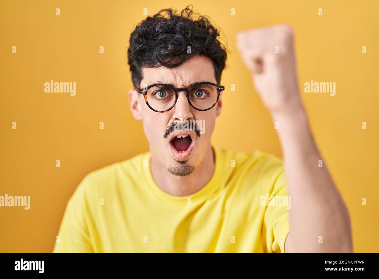 Hispanic man wearing glasses standing over yellow background angry and ...