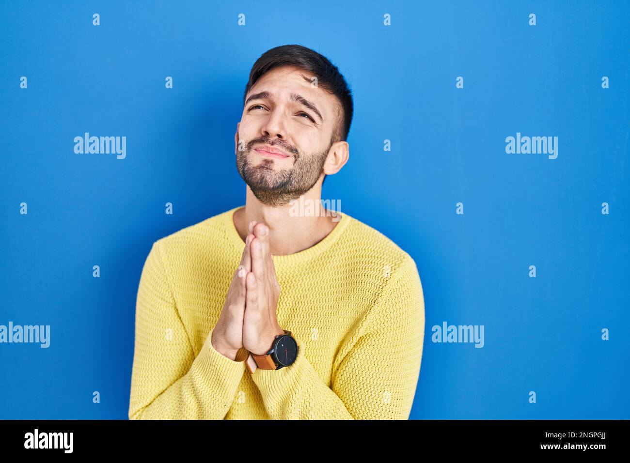 Hispanic man standing over blue background begging and praying with ...