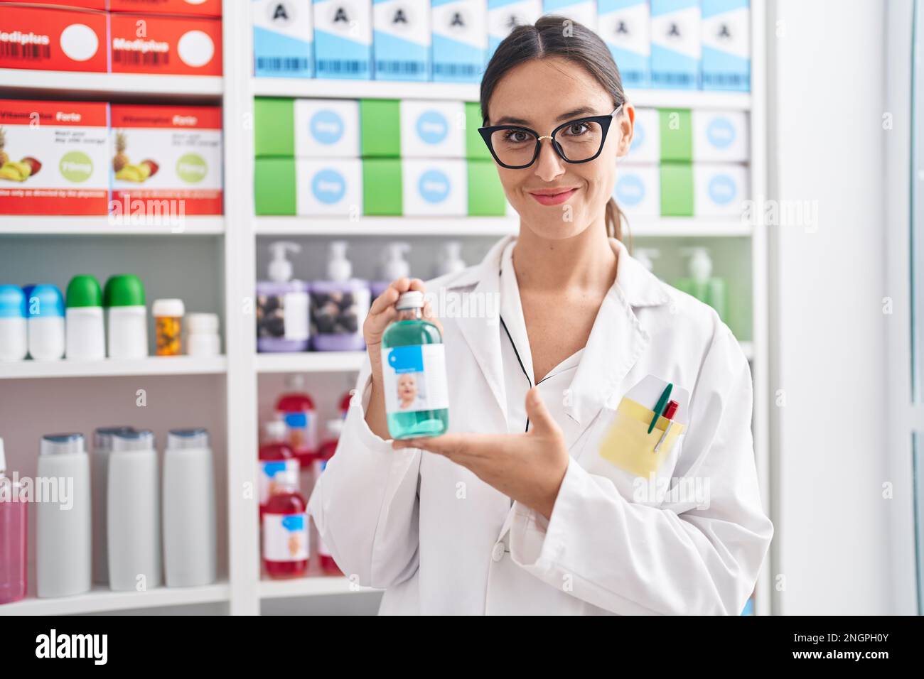 Brunette woman working at pharmacy drugstore holding cough syrup ...