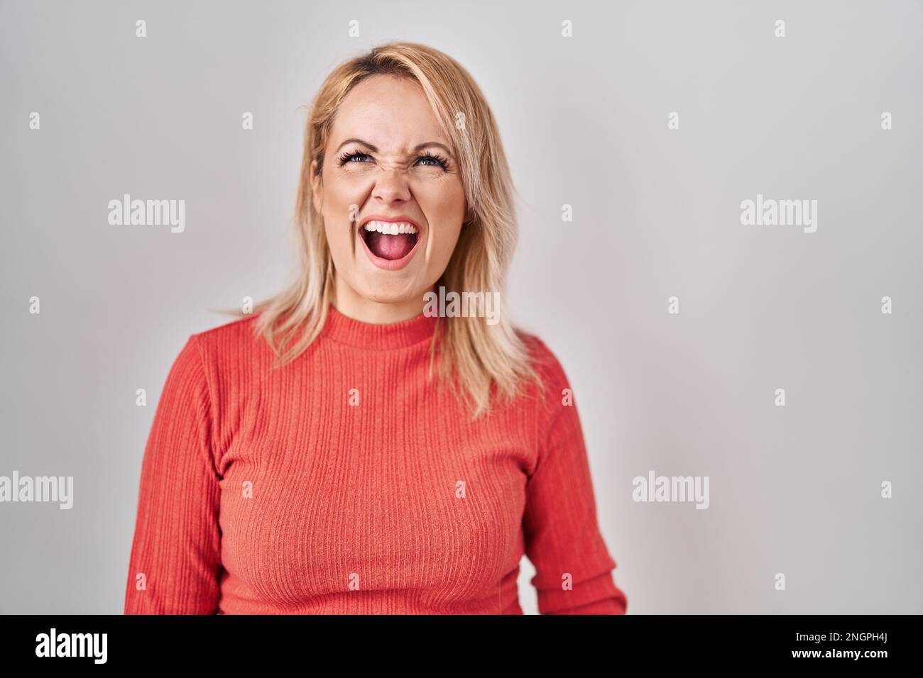 Blonde woman standing over isolated background angry and mad screaming ...