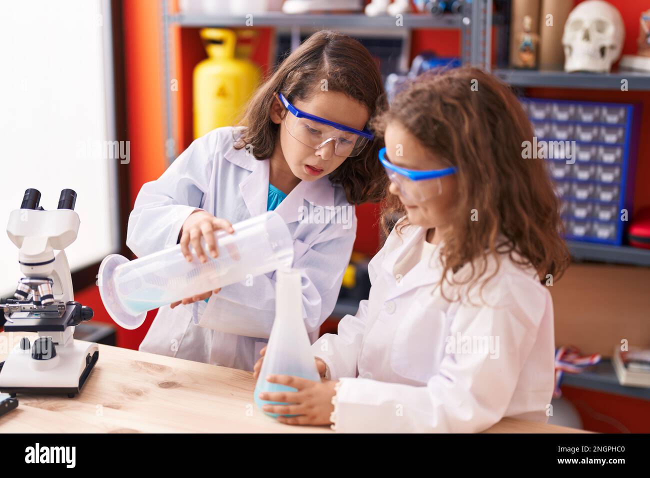 Two kids students pouring liquid on test tube at laboratory classroom ...