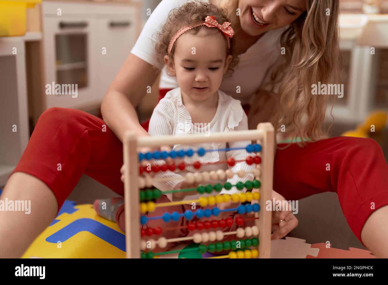 Teacher and toddler learning maths with abacus sitting on floor at ...