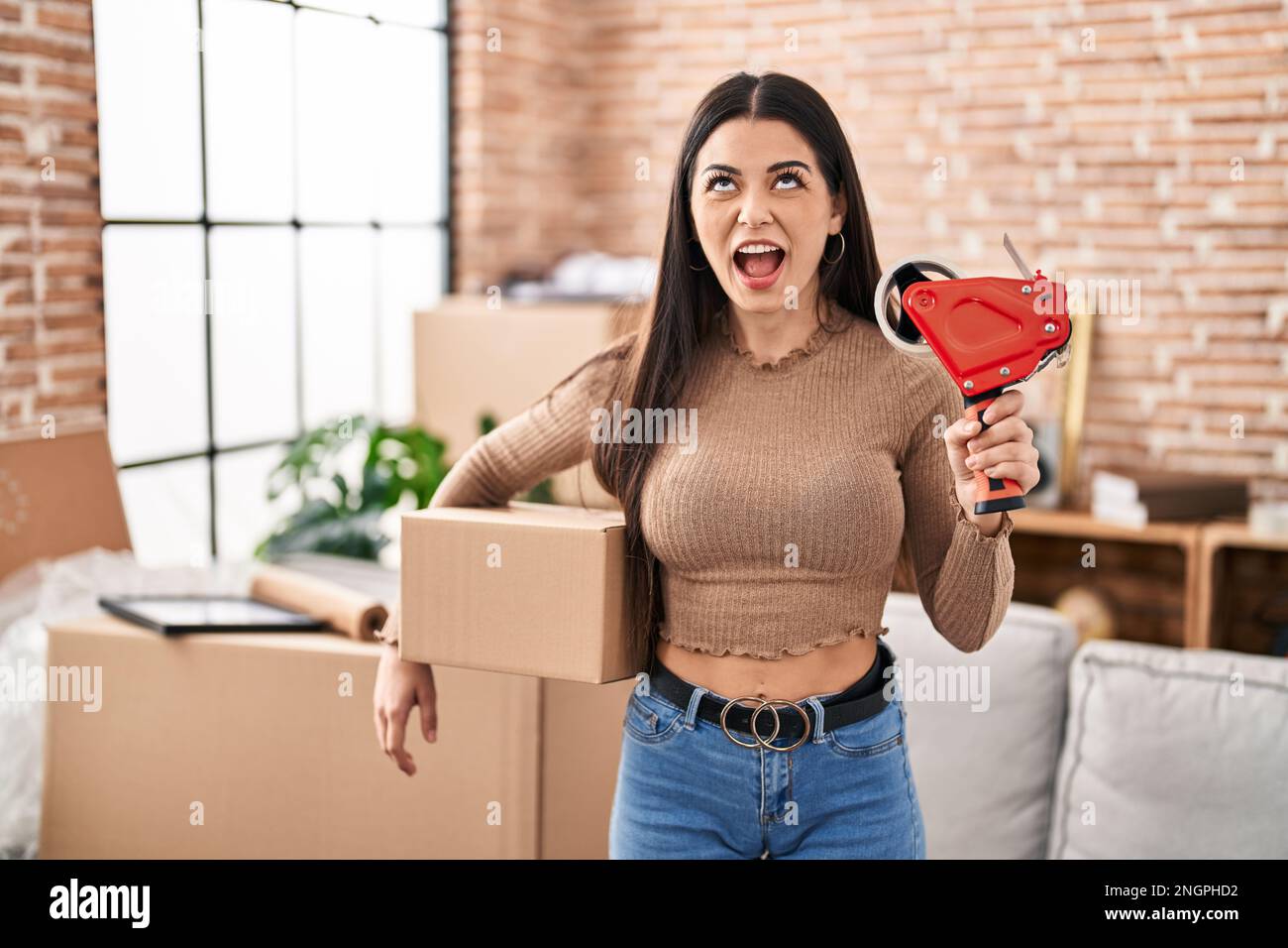 Young woman moving to a new home packing boxes angry and mad screaming ...