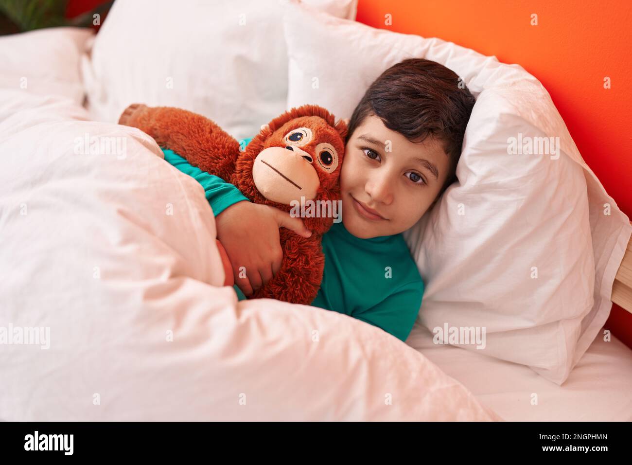 Adorable hispanic boy hugging monkey doll lying on bed at bedroom Stock ...