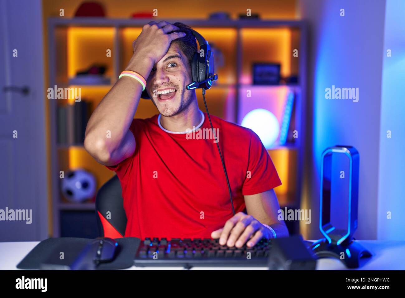 Young hispanic man playing video games surprised with hand on head for ...