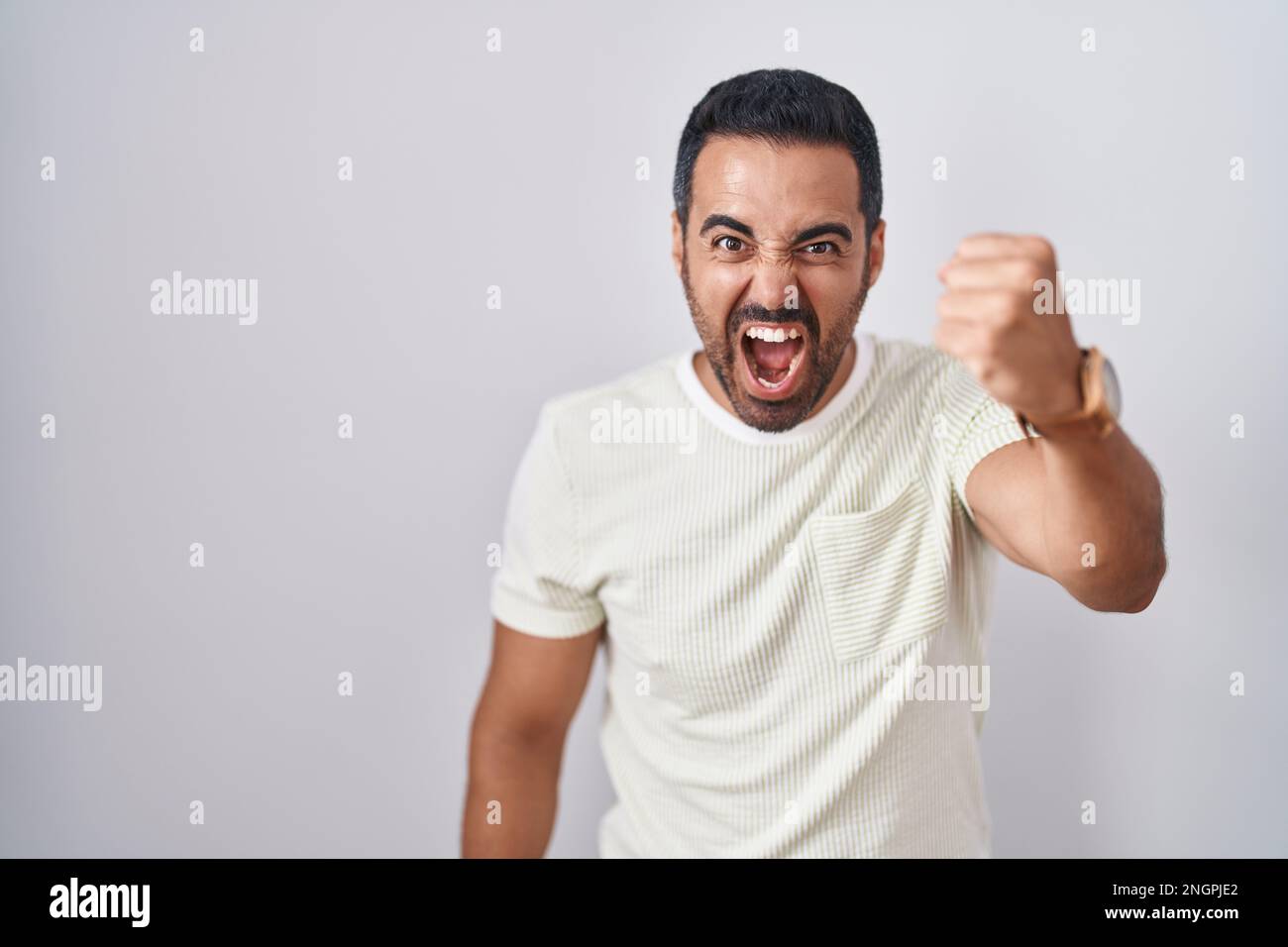 Hispanic man with beard standing over isolated background angry and mad ...