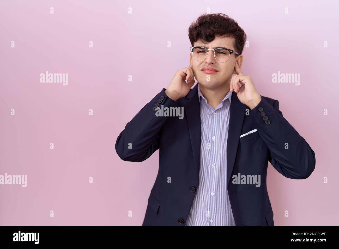 Young non binary man with beard wearing suit and tie covering ears with ...
