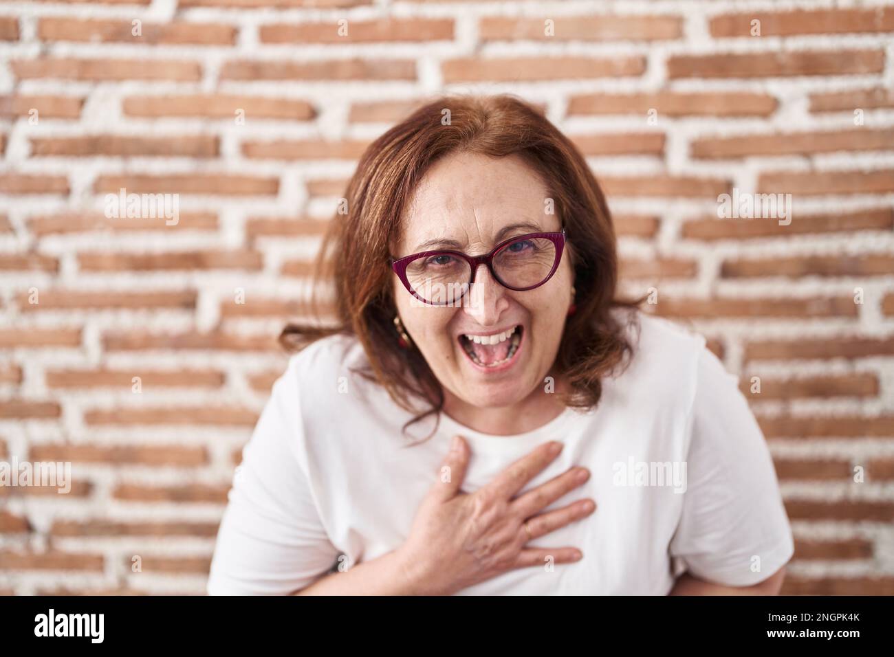 Senior woman with glasses standing over bricks wall smiling and ...