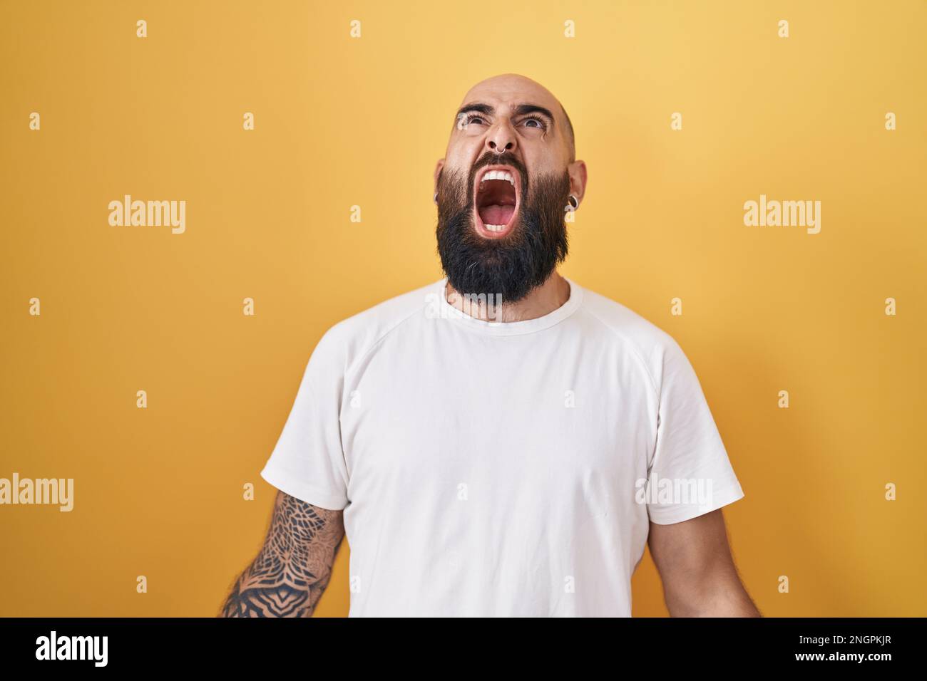 Young hispanic man with beard and tattoos standing over yellow ...