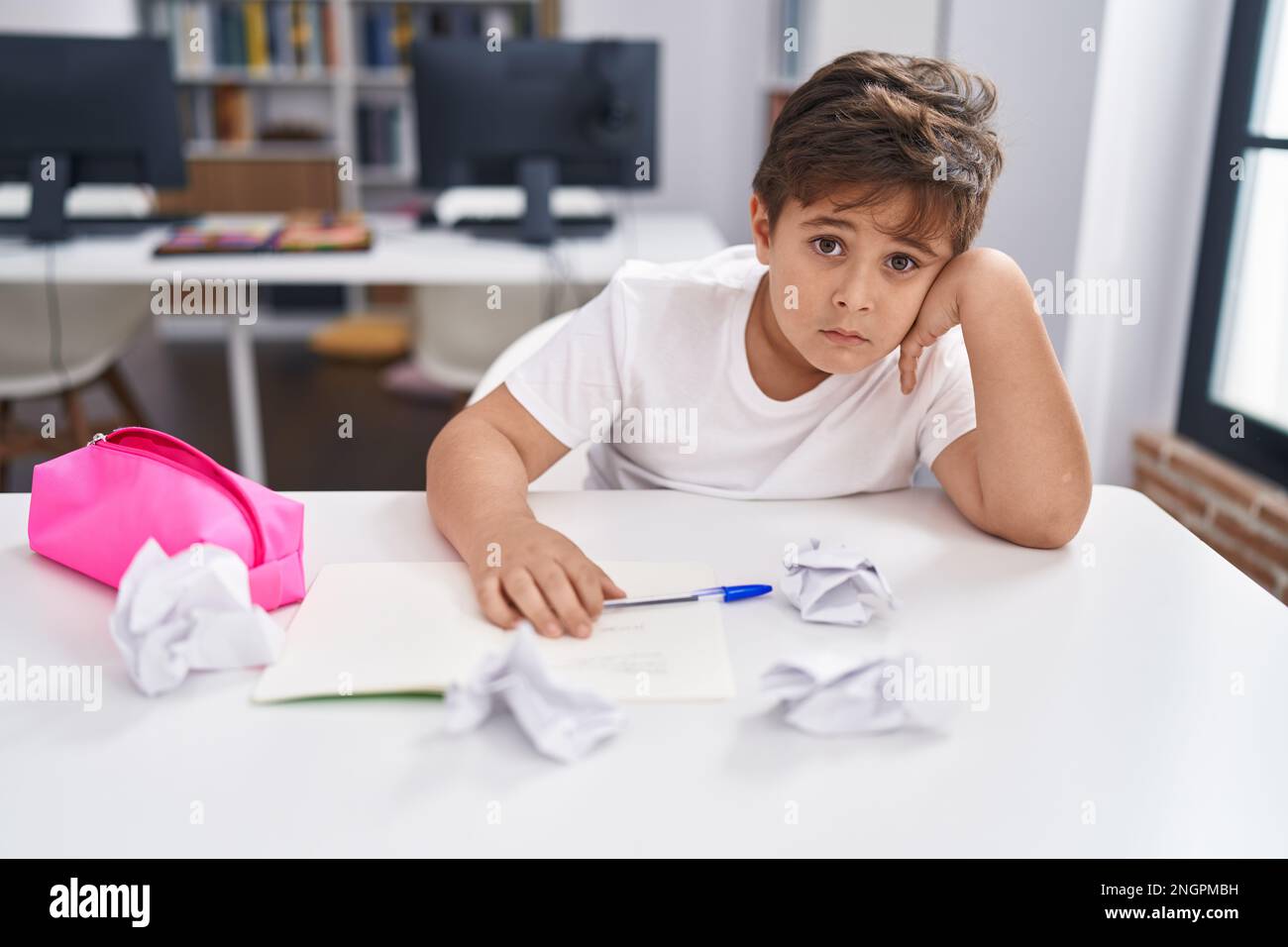 Adorable hispanic boy student sitting on table with worried expression ...