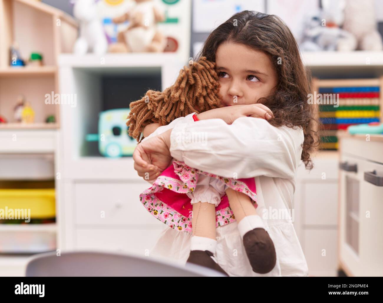 Adorable hispanic girl hugging doll standing at kindergarten Stock ...