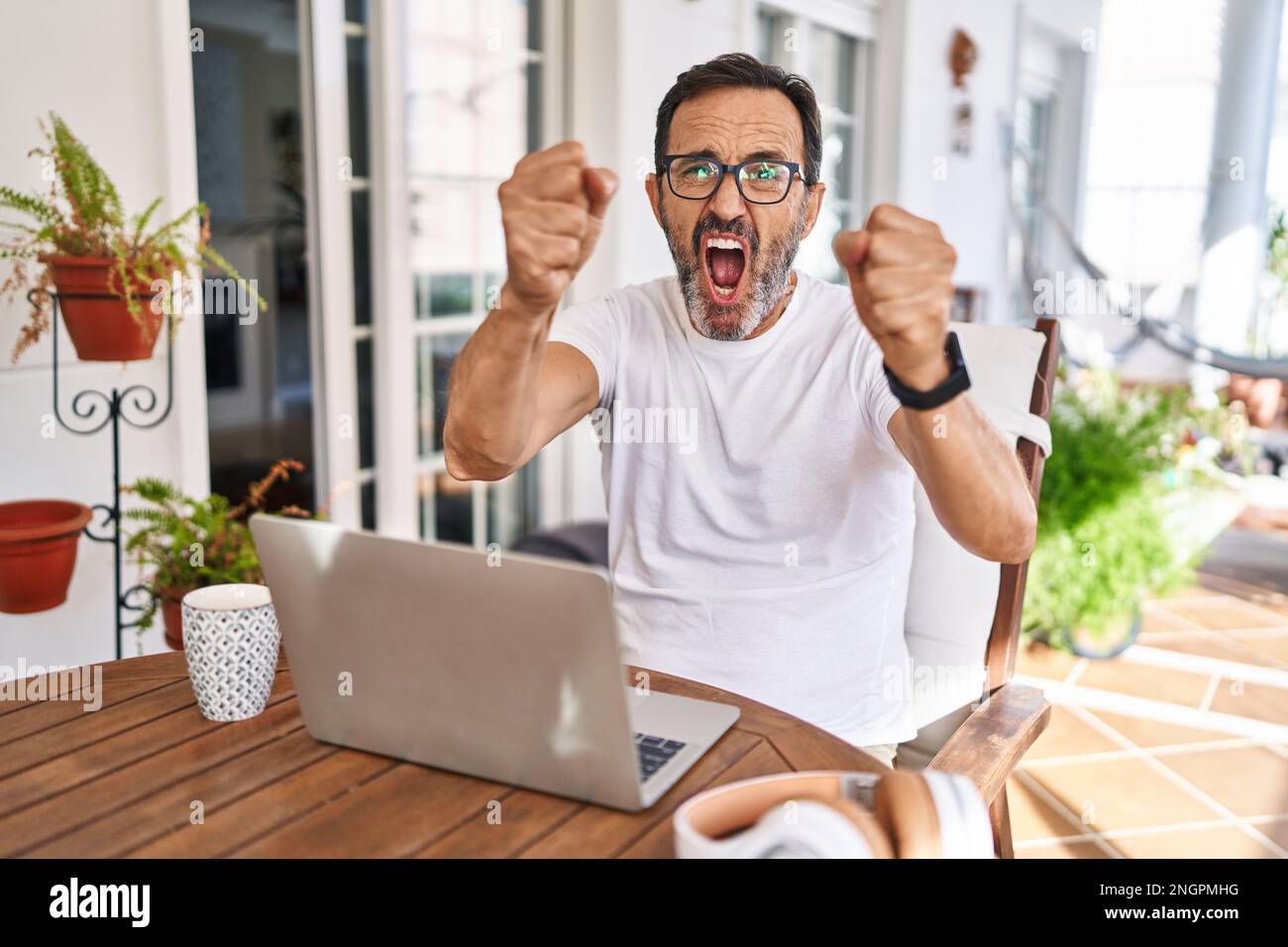 Middle age man using computer laptop at home angry and mad raising ...