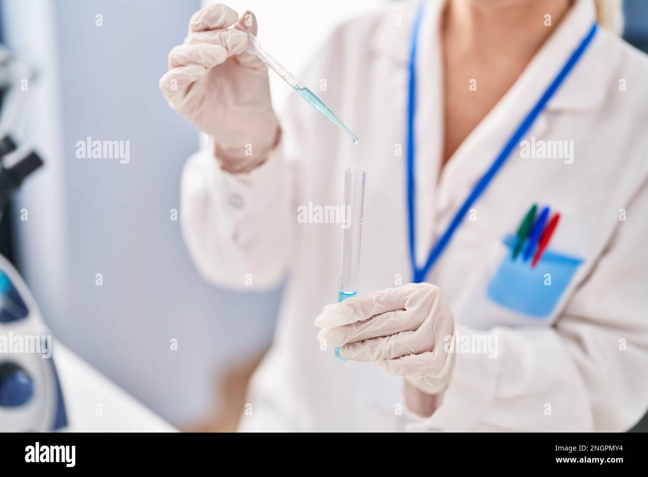 Young blonde woman wearing scientist uniform measuring liquid at ...