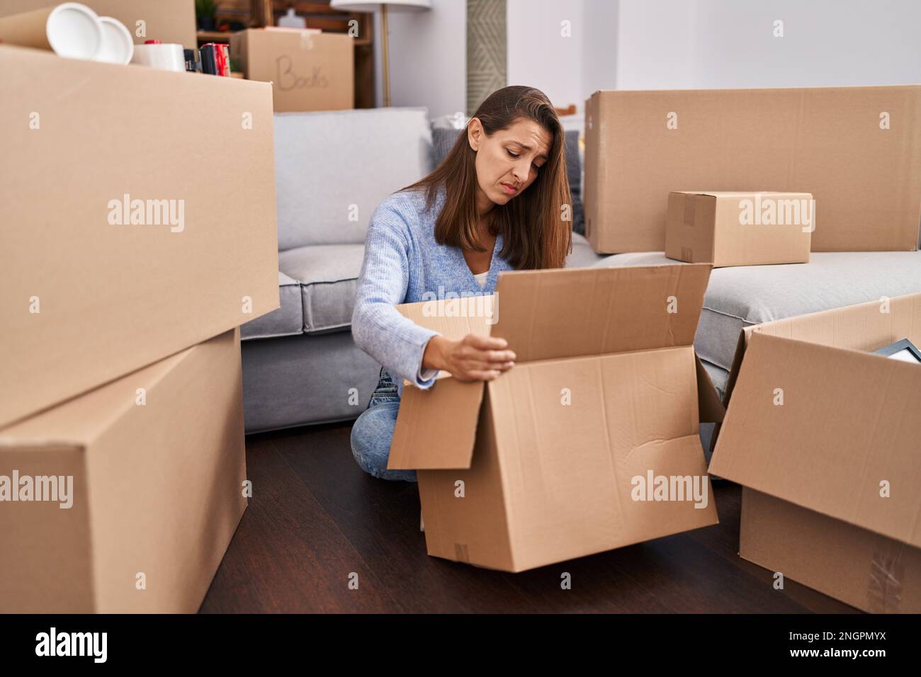 Young woman moving to a new home looking inside cardboard box depressed ...